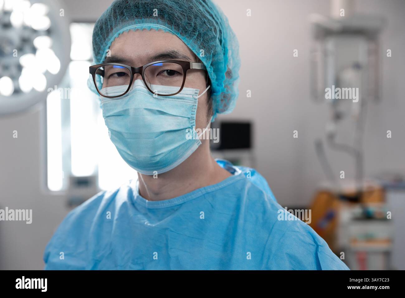 Asian male surgeon standing attentively in operating room with surgical ...