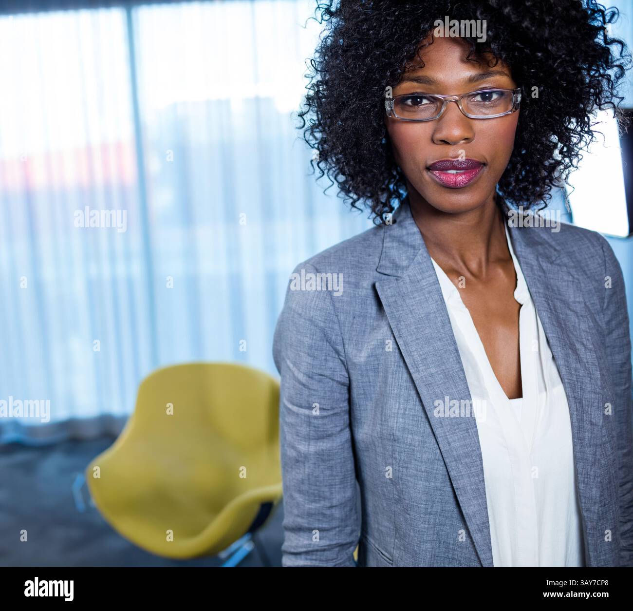 African American woman standing in office lounge by sheer curtains and ...