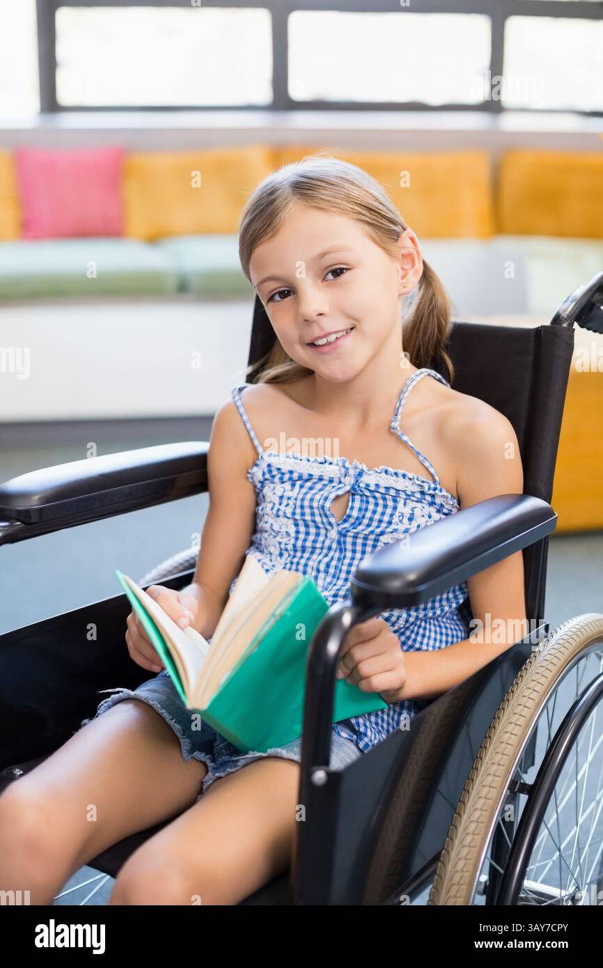 Girl child sitting in wheelchair reading green book in living room ...