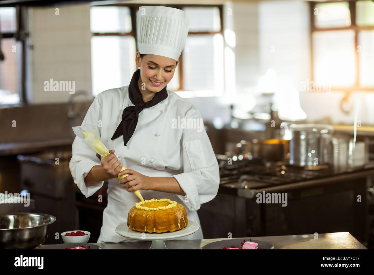 Female pastry chef piping icing onto bundt cake in commercial kitchen ...