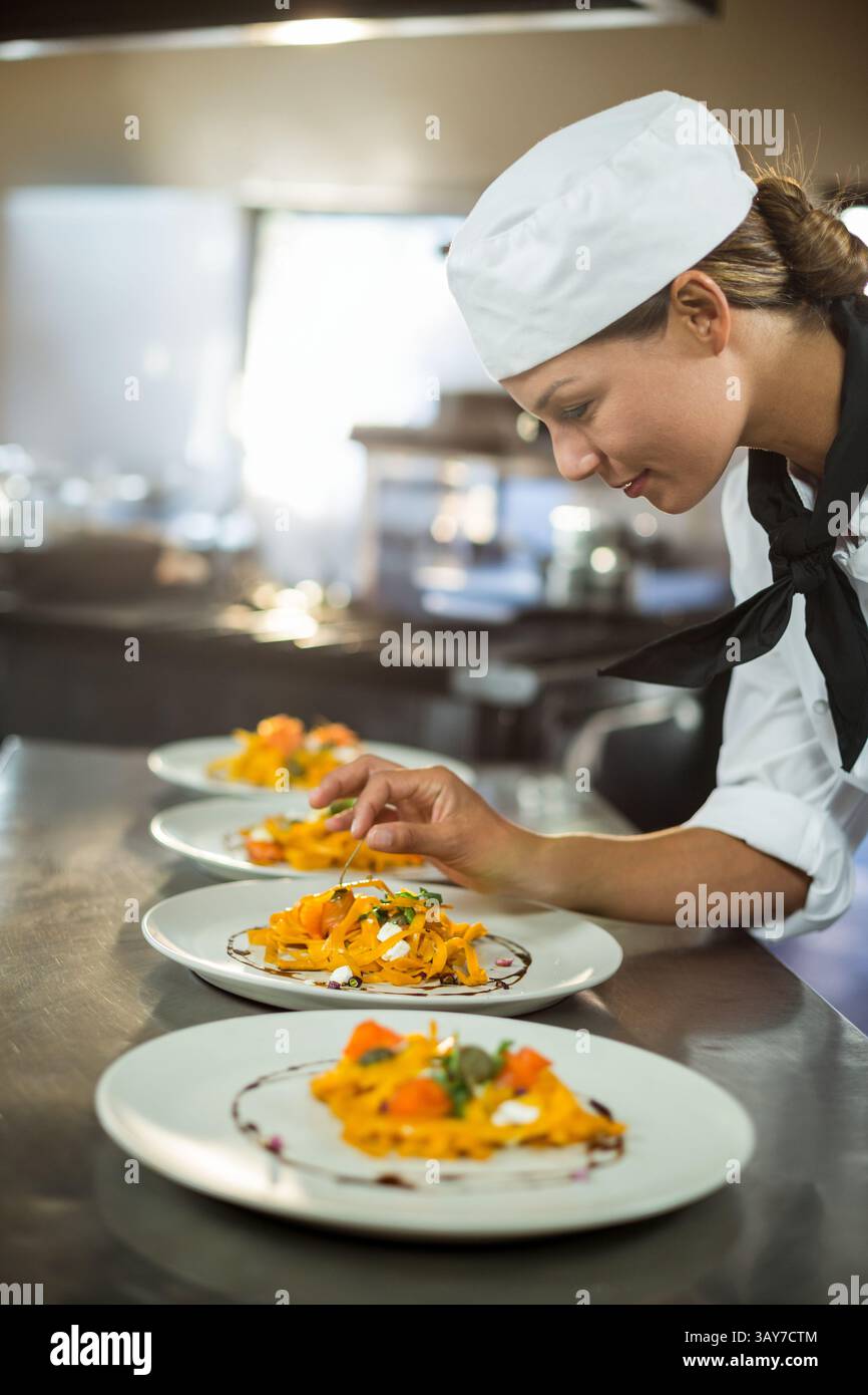 Asian female chef carefully garnishing pasta plates in commercial ...