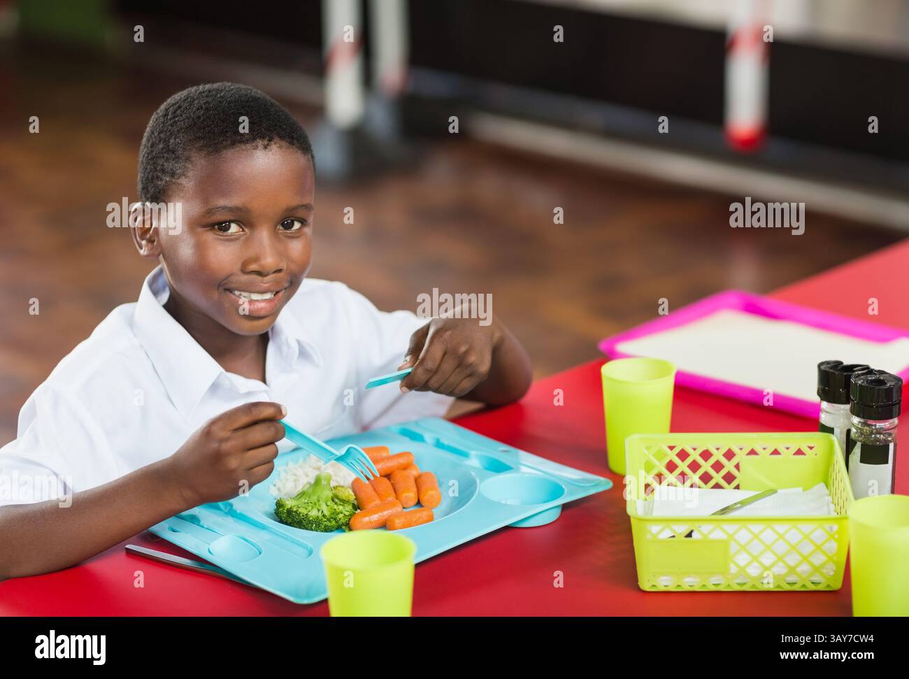 African American boy eating lunch at red cafeteria table, using blue ...
