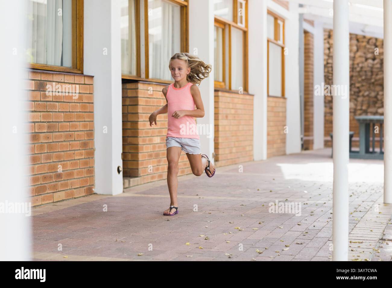 Girl running along covered brick corridor at school, with wooden ...