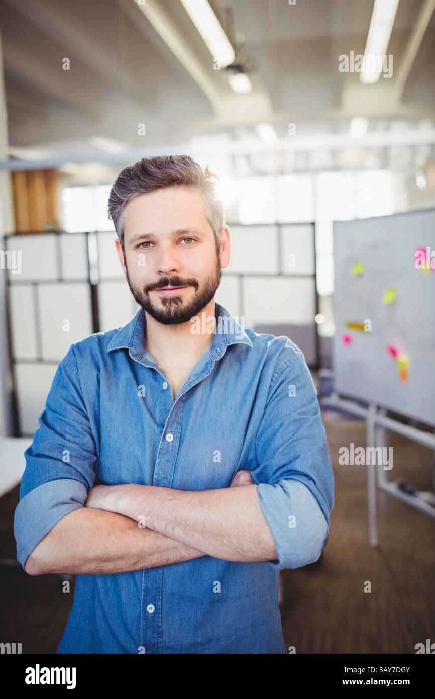 Man standing with arms crossed in open-plan office, with whiteboard ...