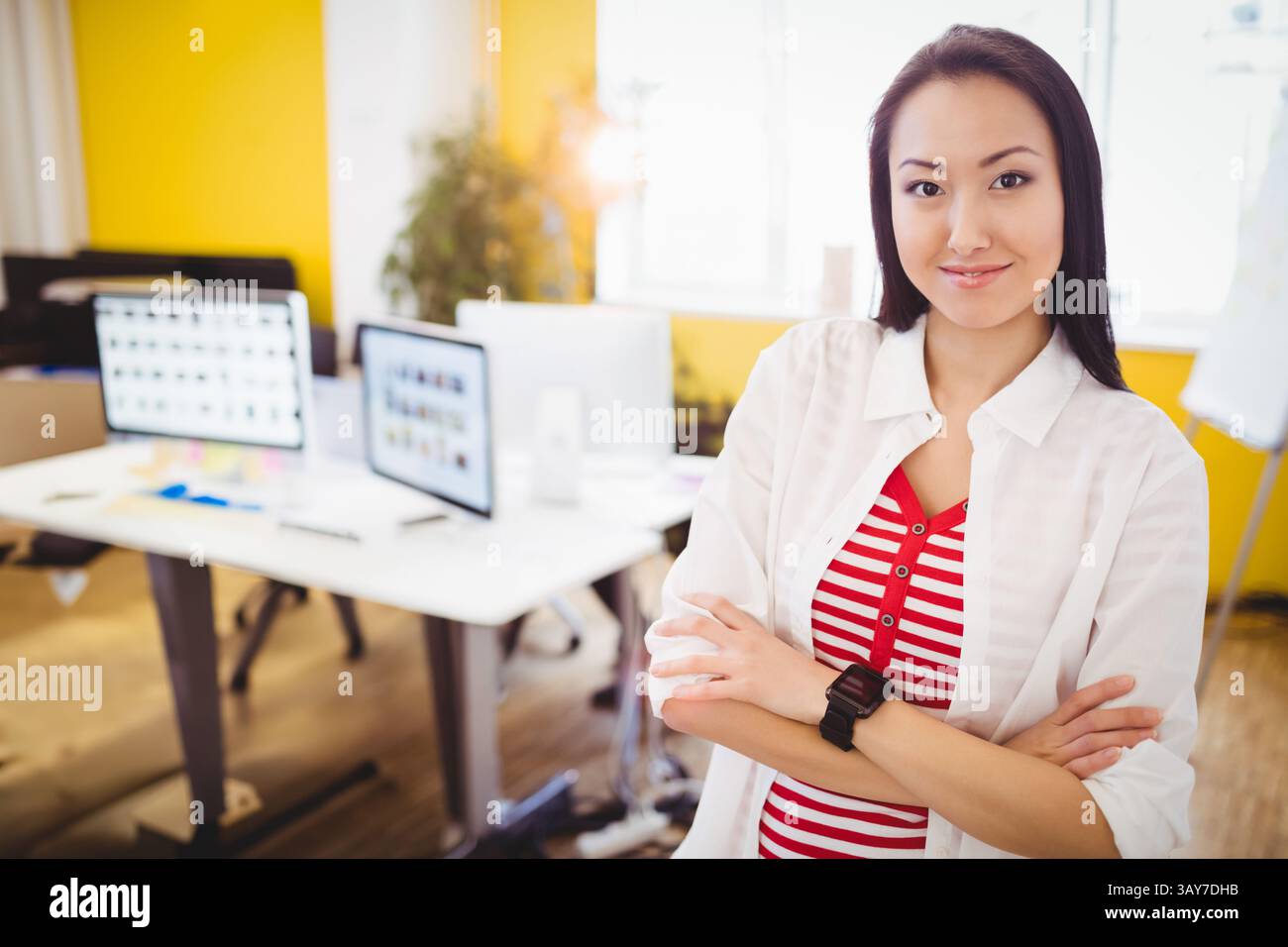 Young Asian woman standing with arms crossed smiling in open-plan ...