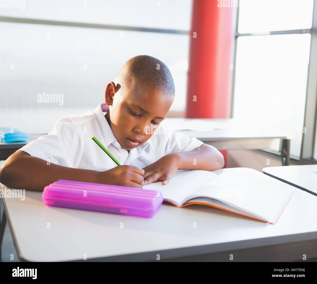 African American boy writing in notebook in classroom, using green ...