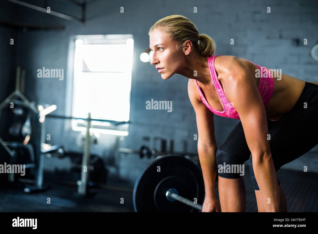 Woman gripping loaded barbell on rubber flooring in weightlifting area ...