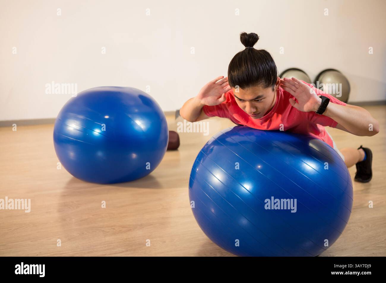 Asian woman leaning forward on blue stability ball in fitness studio ...