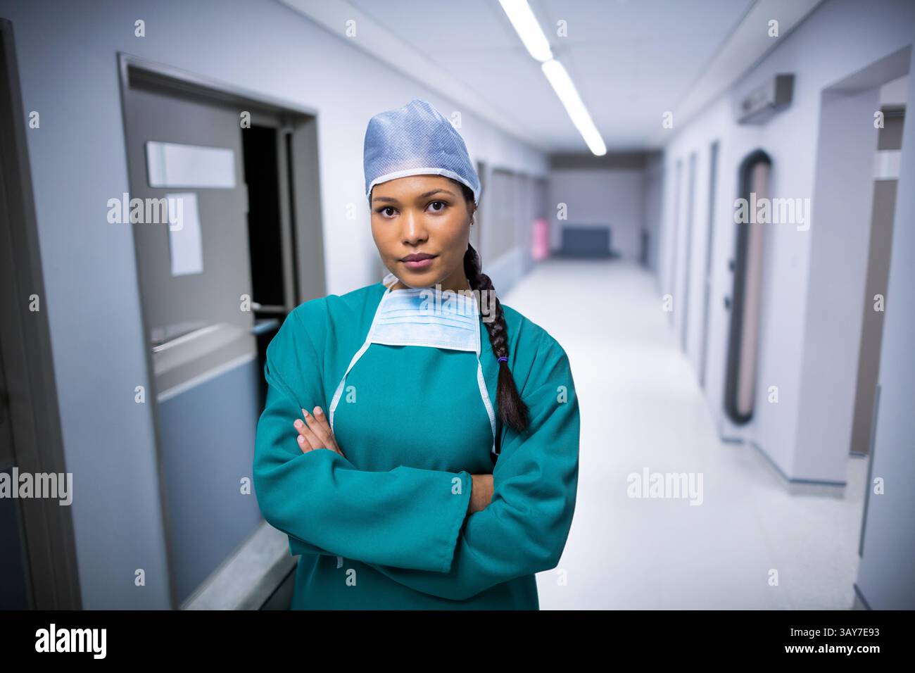 Female surgeon standing with arms crossed in hospital corridor, wearing ...