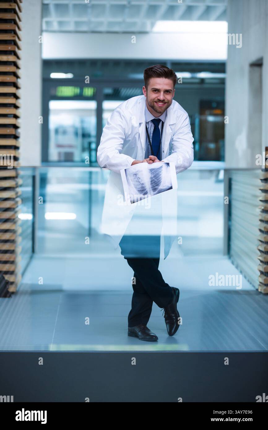 Male doctor leaning against glass railing in modern hospital atrium ...