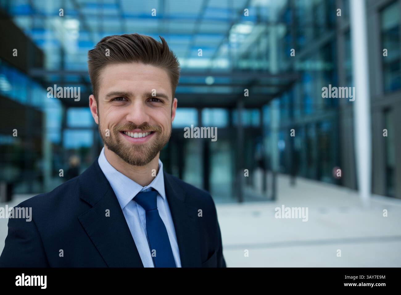 Man wearing suit, blue tie standing smiling outside office entrance ...