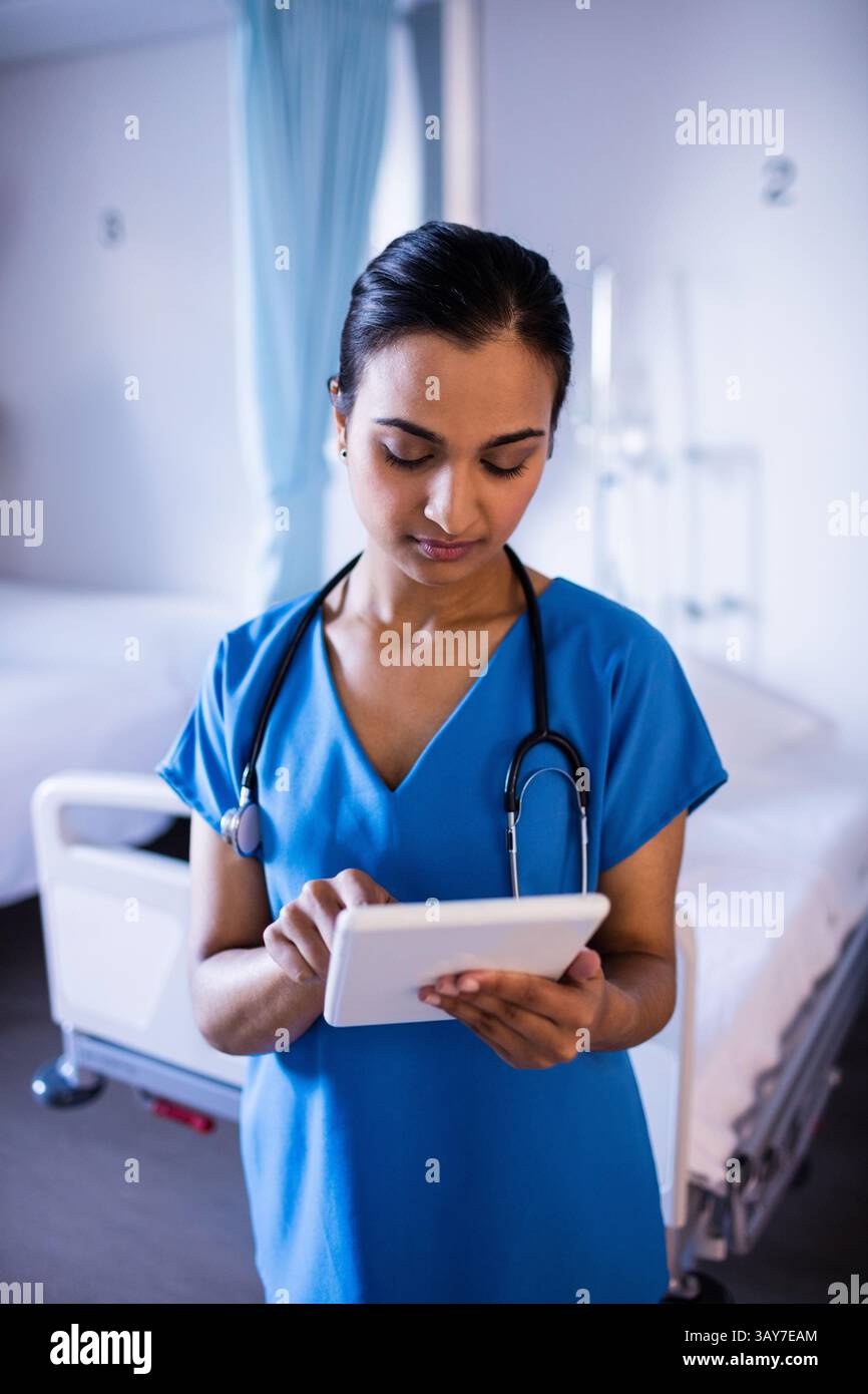 Young Indian nurse standing in hospital room, checking tablet with ...