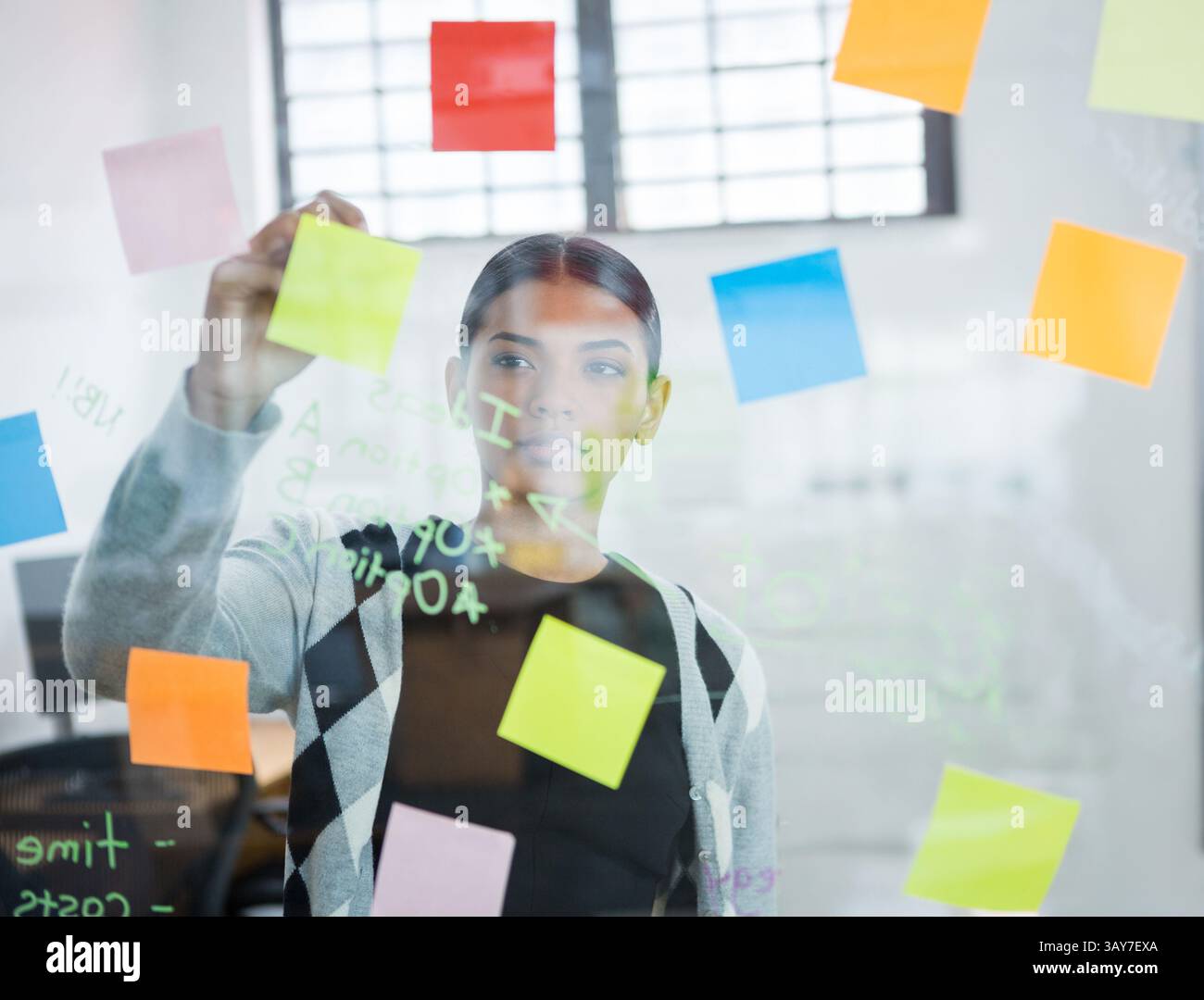 Woman arranging colorful sticky notes on glass board in open-plan ...