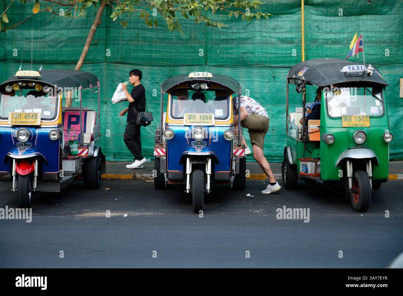 Colorful tuk-tuks lined up on a Bangkok street as a tourist hops in Stock Photo - Alamy