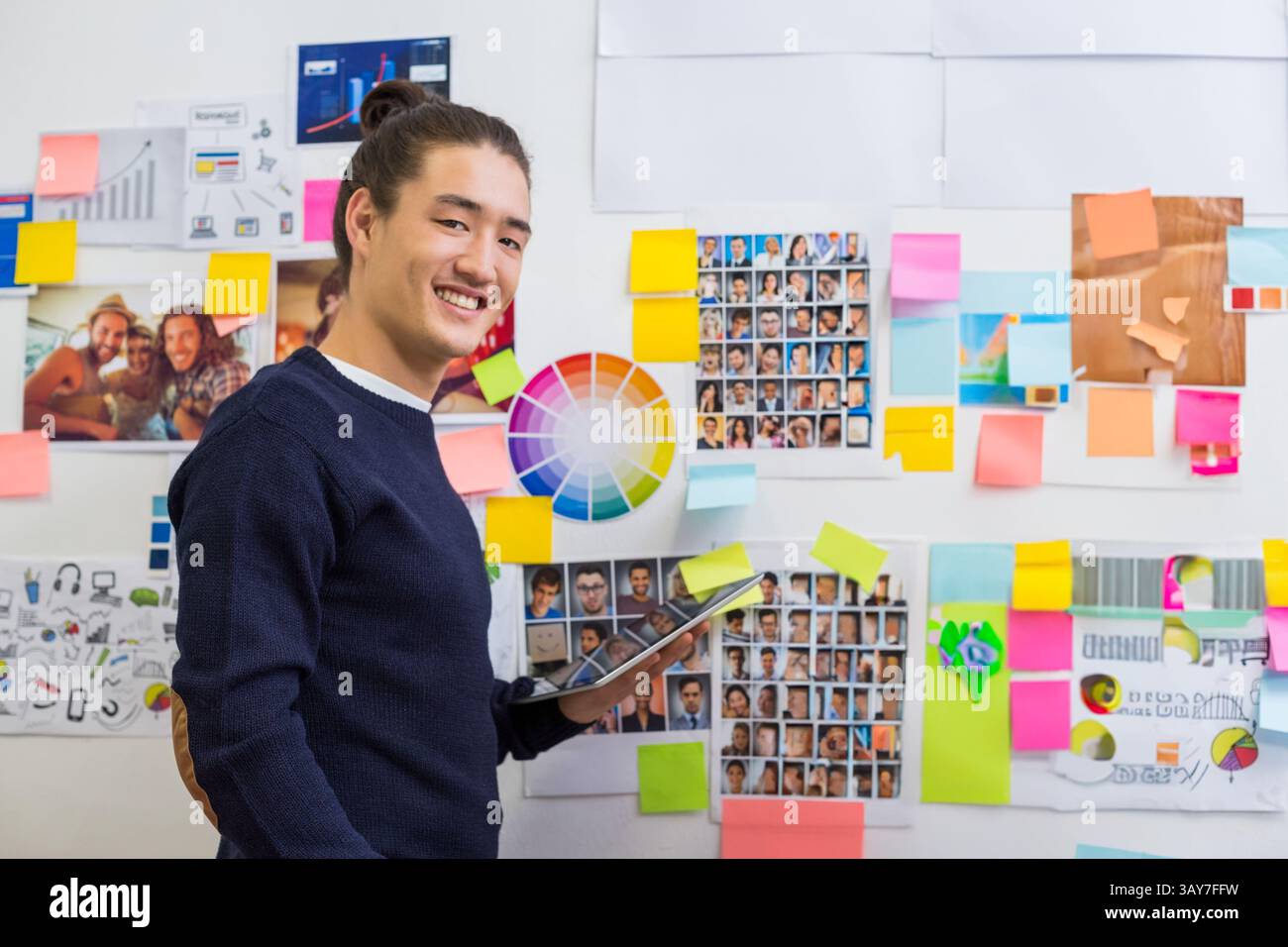 Asian man standing in creative studio, reviewing ideas on tablet with ...