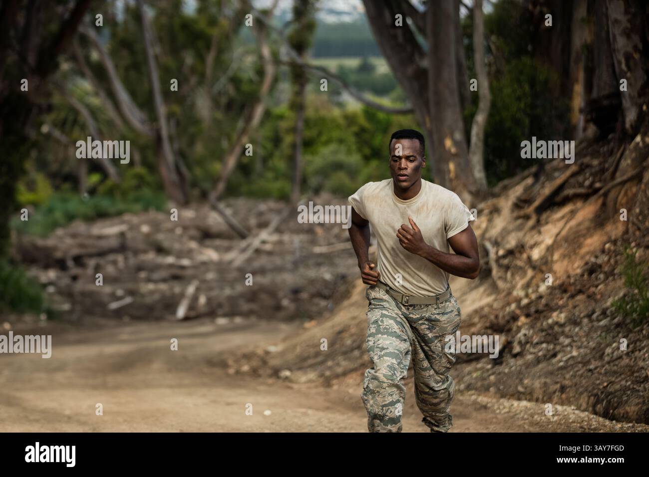 African American man running on dirt trail in forest, dodging exposed ...