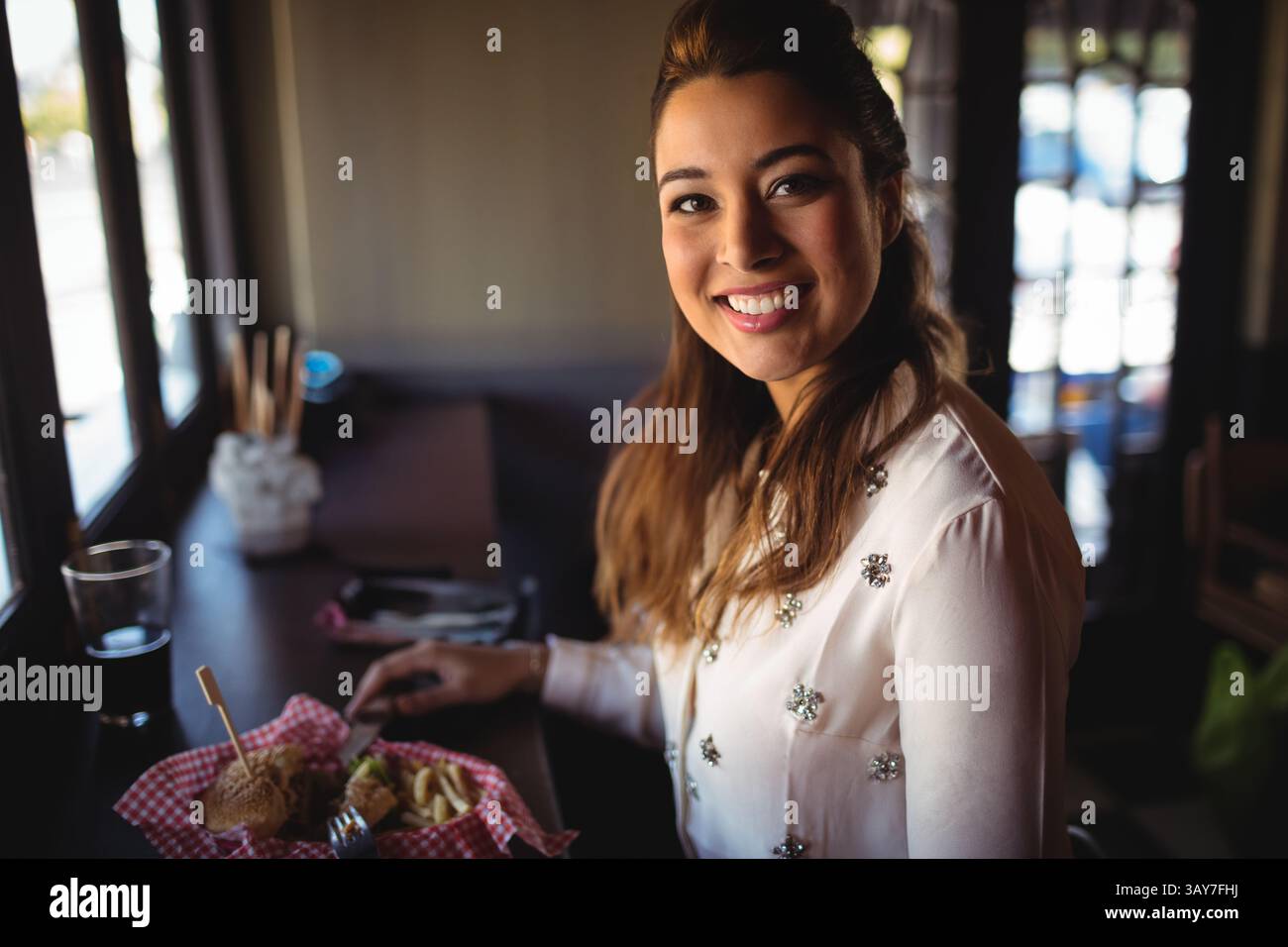 Young woman sitting at counter by window in café, eating fries from ...
