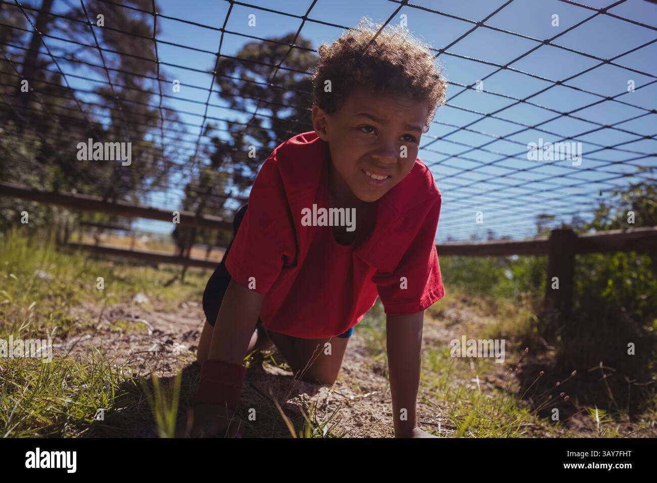 Child crawling under net at outdoor obstacle course, with wooden posts and wrist guards ...