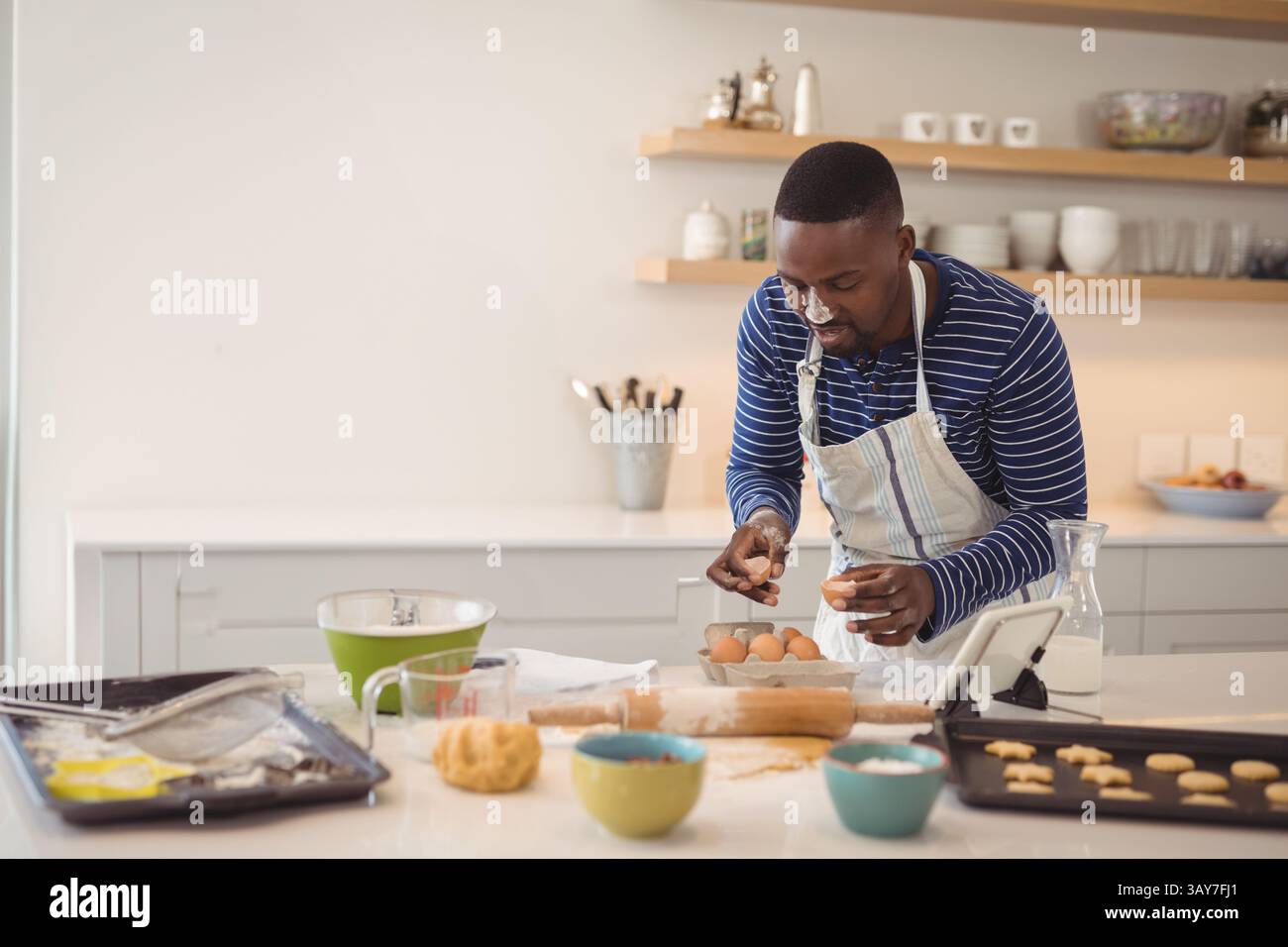 African American man cracking eggs in modern home kitchen, with egg ...
