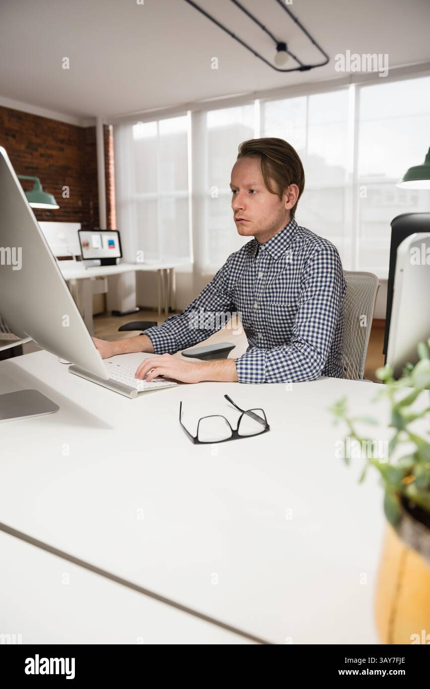 Man typing on keyboard by monitor at open-plan office desk, with ...