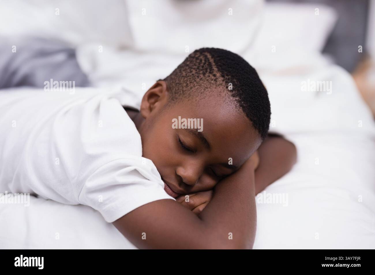African American boy sleeping on white bed in bedroom at home, with ...