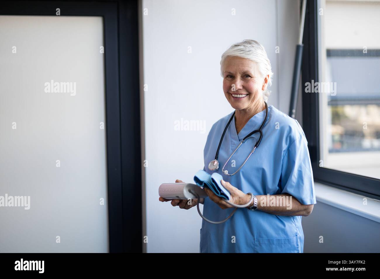 Senior female nurse holding blood pressure monitor and cuff at clinic ...