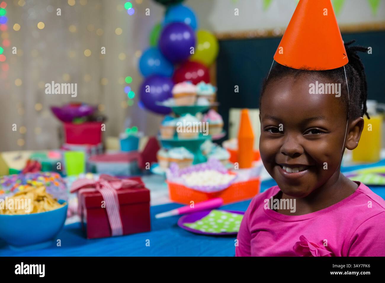 African American boy sitting at birthday party table, wearing party hat ...