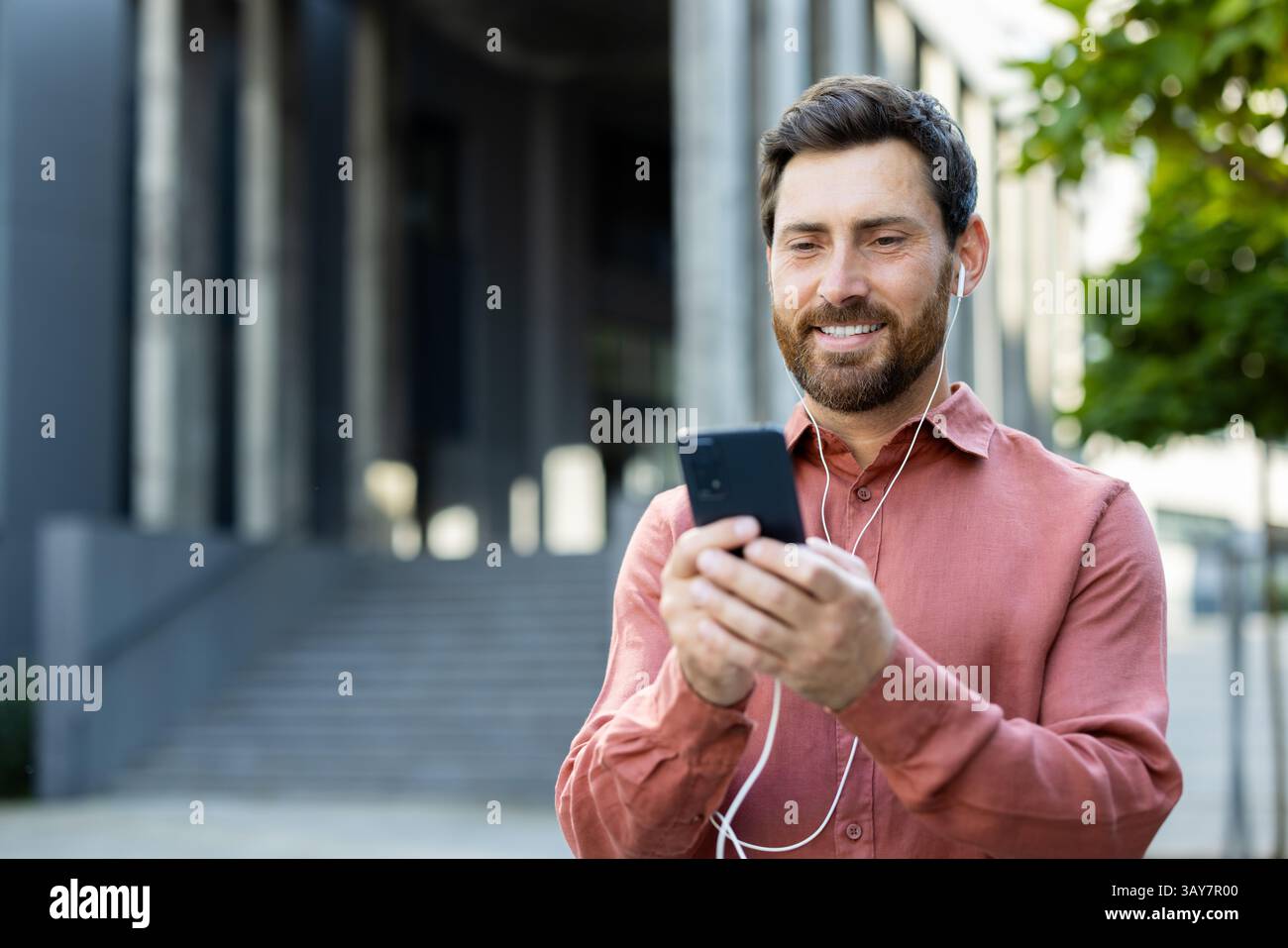 A smiling man uses his smartphone while wearing earbuds, captured ...