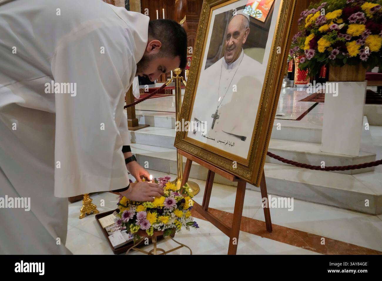 An altar server sets a candle in front of a portrait of the late Pope ...