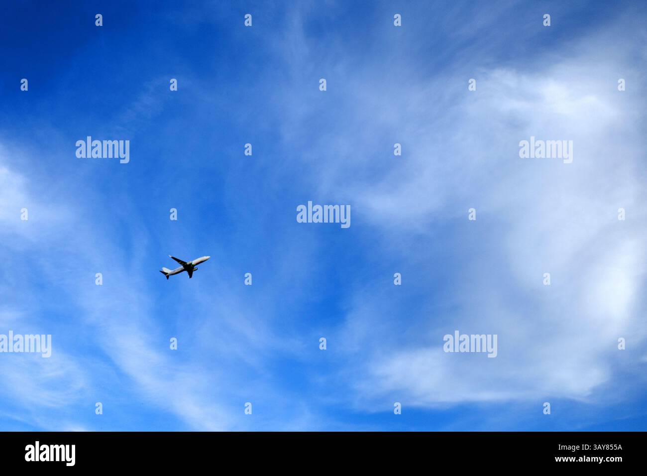 Airplane flying in a clear blue sky with wispy white clouds. The ...