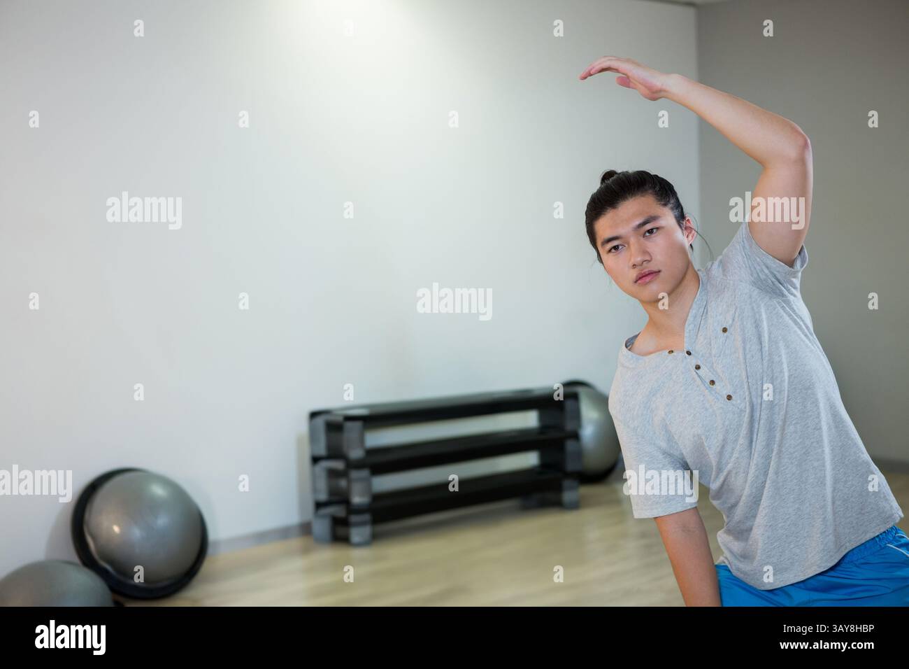 Young Asian woman performing side stretch in gym, exercise balls, step ...