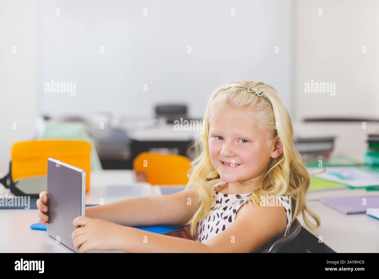 Six-year-old girl holding tablet and sitting at desk in elementary classroom, copy space Stock ...