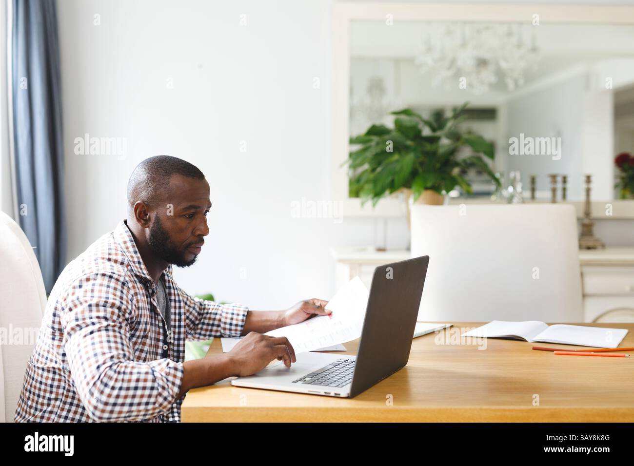 African American man typing on laptop and reviewing documents at dining ...