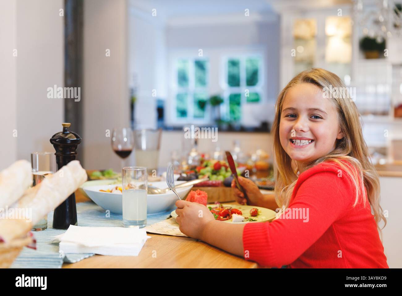 Seven-year-old girl sitting at dining table in kitchen, with salad bowl ...