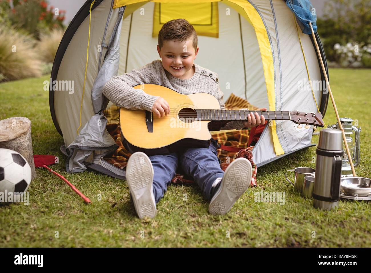 child boy strumming acoustic guitar in backyard, with yellow-gray tent ...