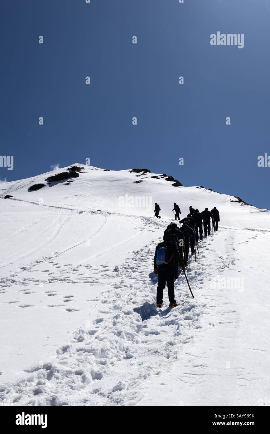 team of hikers trekking to snowy peak summit under clear blue sky in daylight image is taken at ...