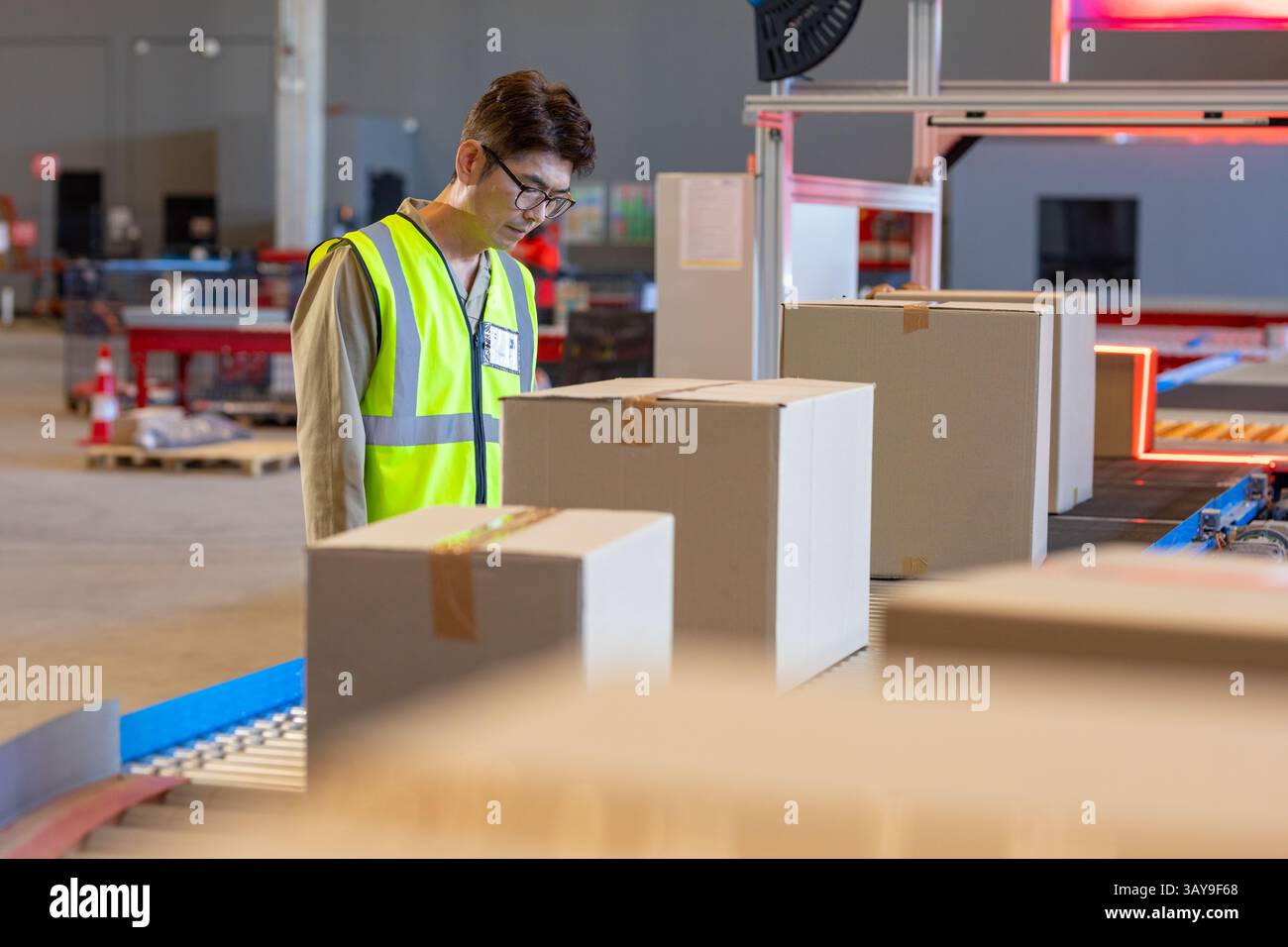 Korean man inspecting boxes on conveyor belt in warehouse, with ...