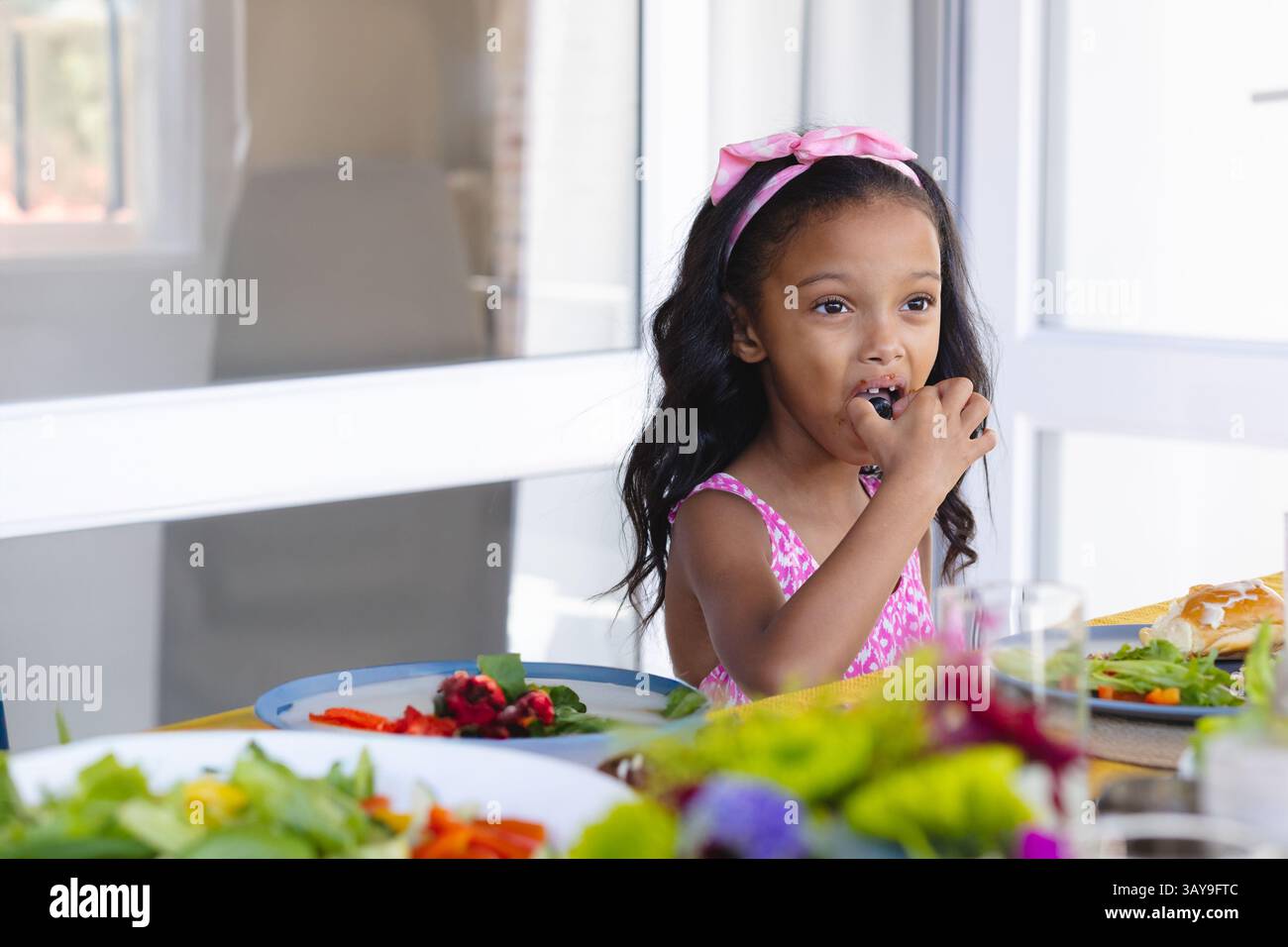Girl eating berry at dining table in bright modern room, with colorful ...
