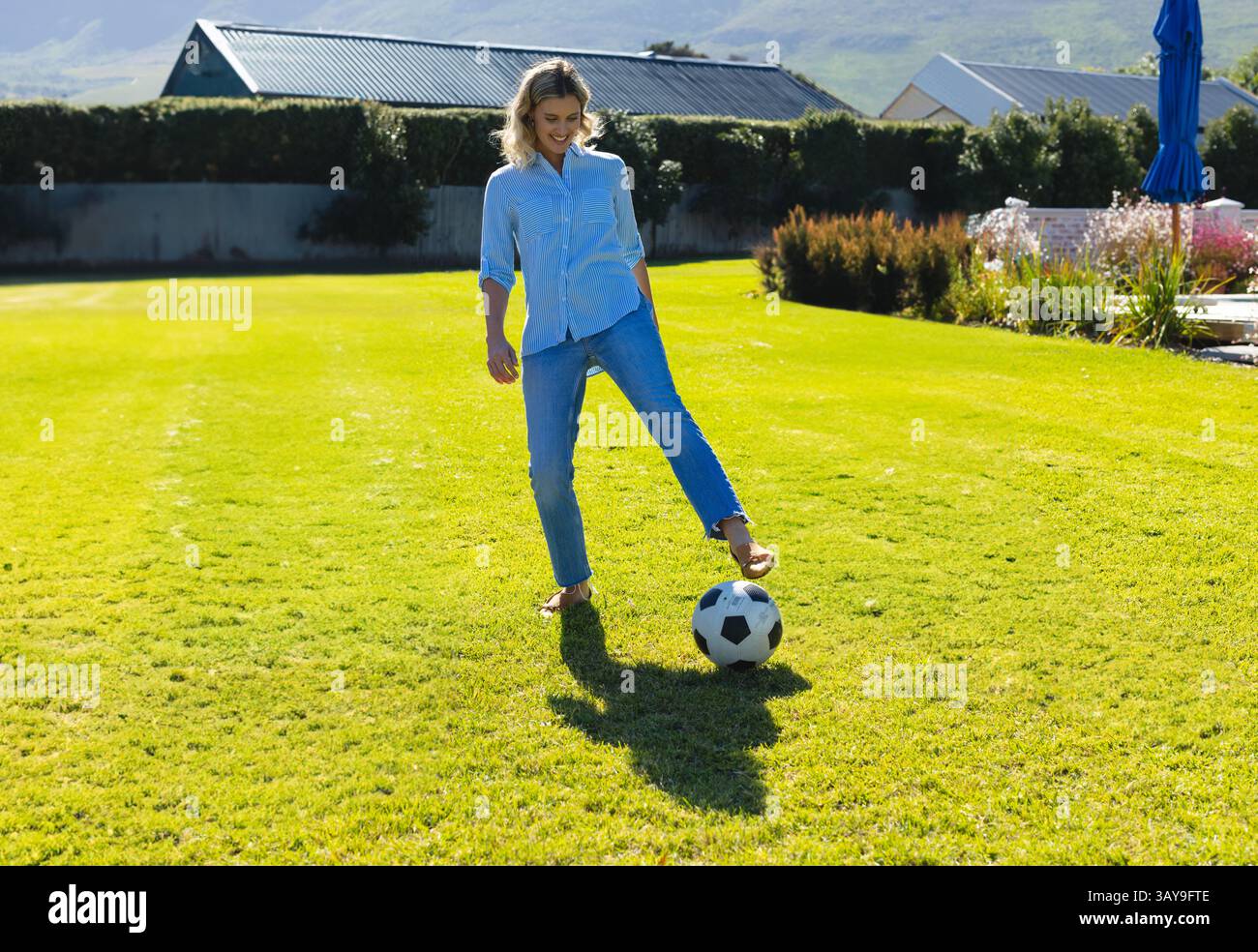 Woman kicking black-and-white soccer ball on backyard lawn, with ...