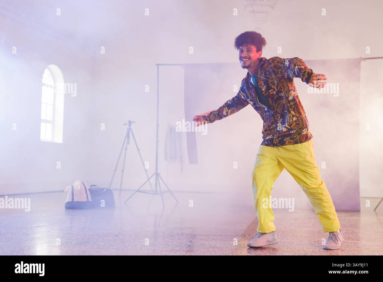 Man dancing energetically in hazy studio, with tripod, backdrop stand ...