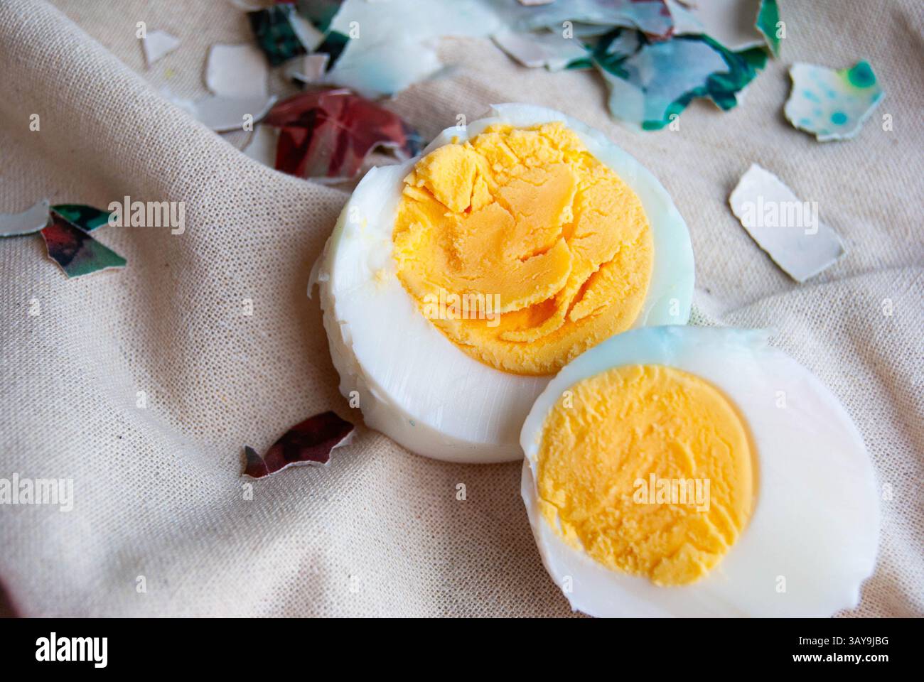 Two hard-boiled eggs placed on a plain background, surrounded by fragments of colorful cracked ...