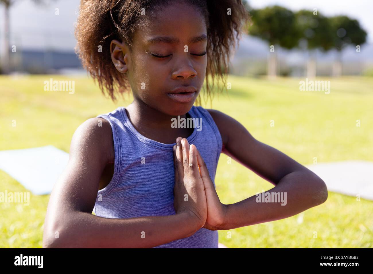 African American child girl meditating on yoga mat in public park ...