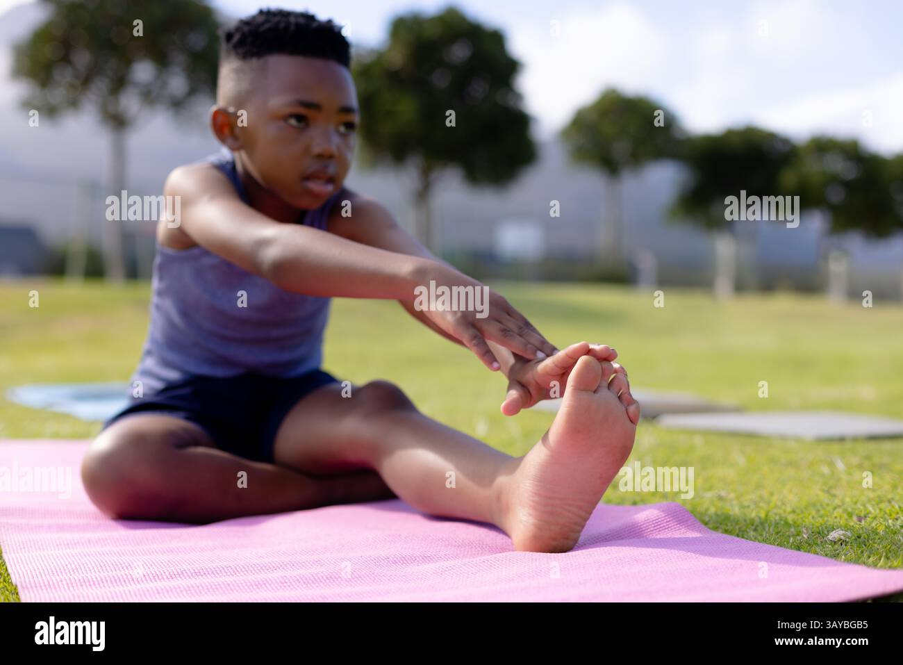 African American child boy stretching forward on pink mat in park ...