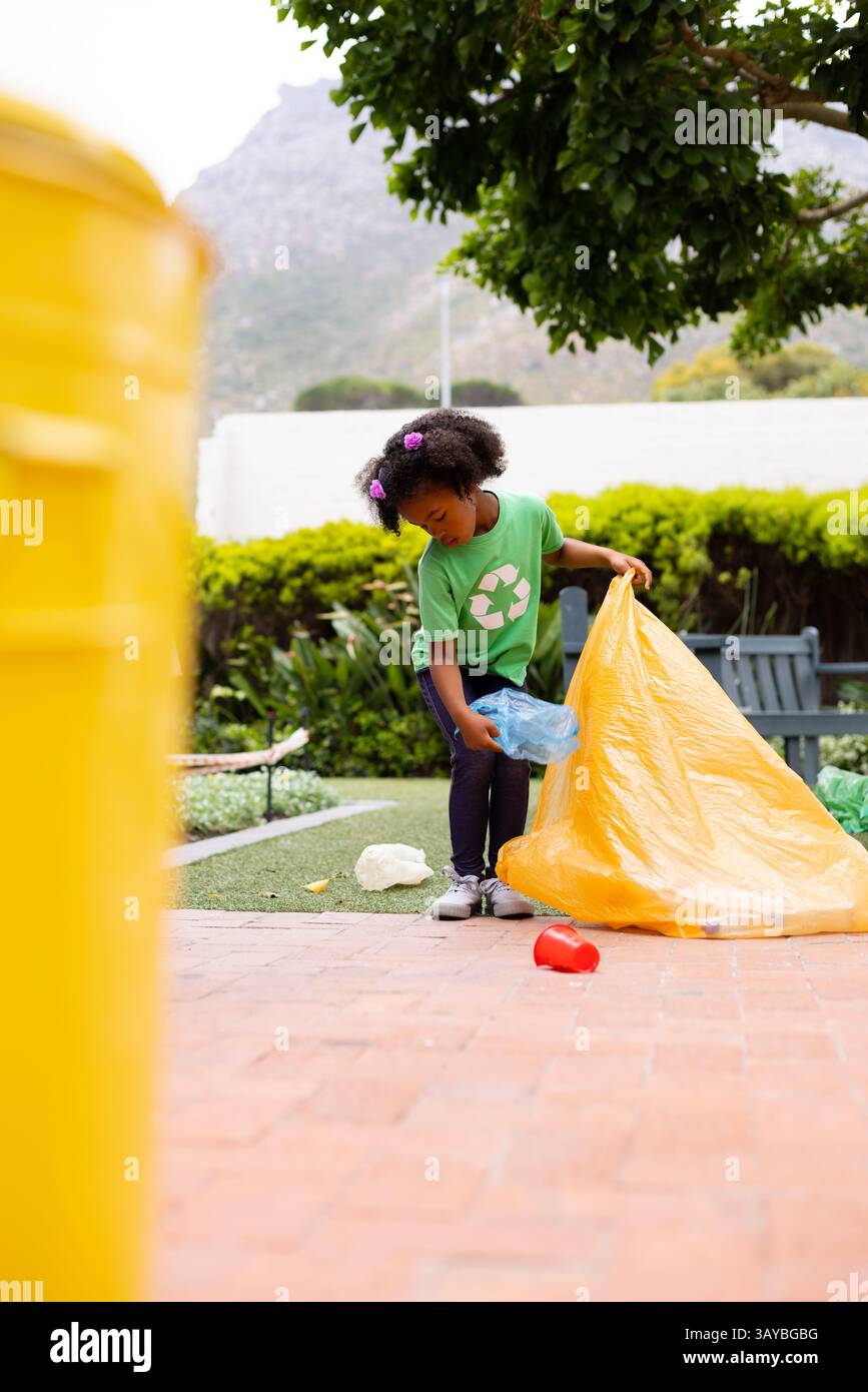African American girl picking up blue plastic on red brick patio with ...