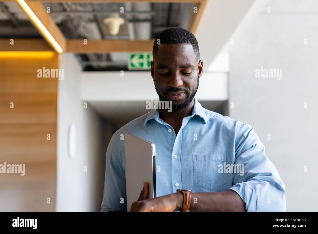 African American man checking wristwatch while holding laptop in office ...