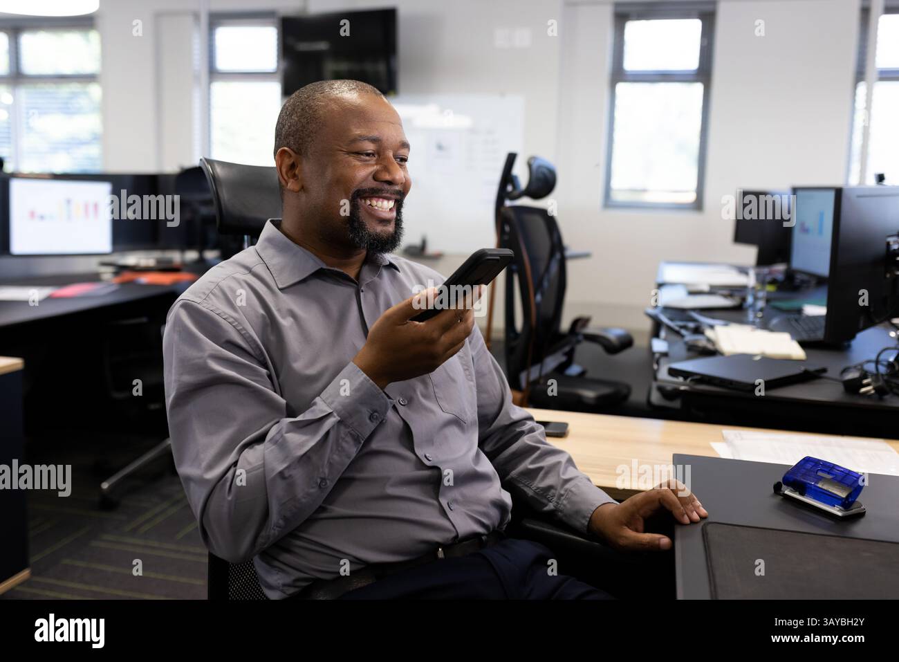 Mature African American man speaking on smartphone in open plan office ...
