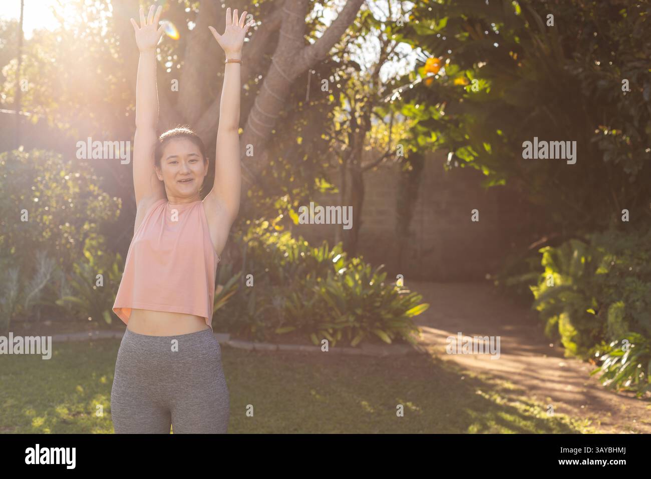 Asian woman stretching arms overhead on grassy lawn in residential ...