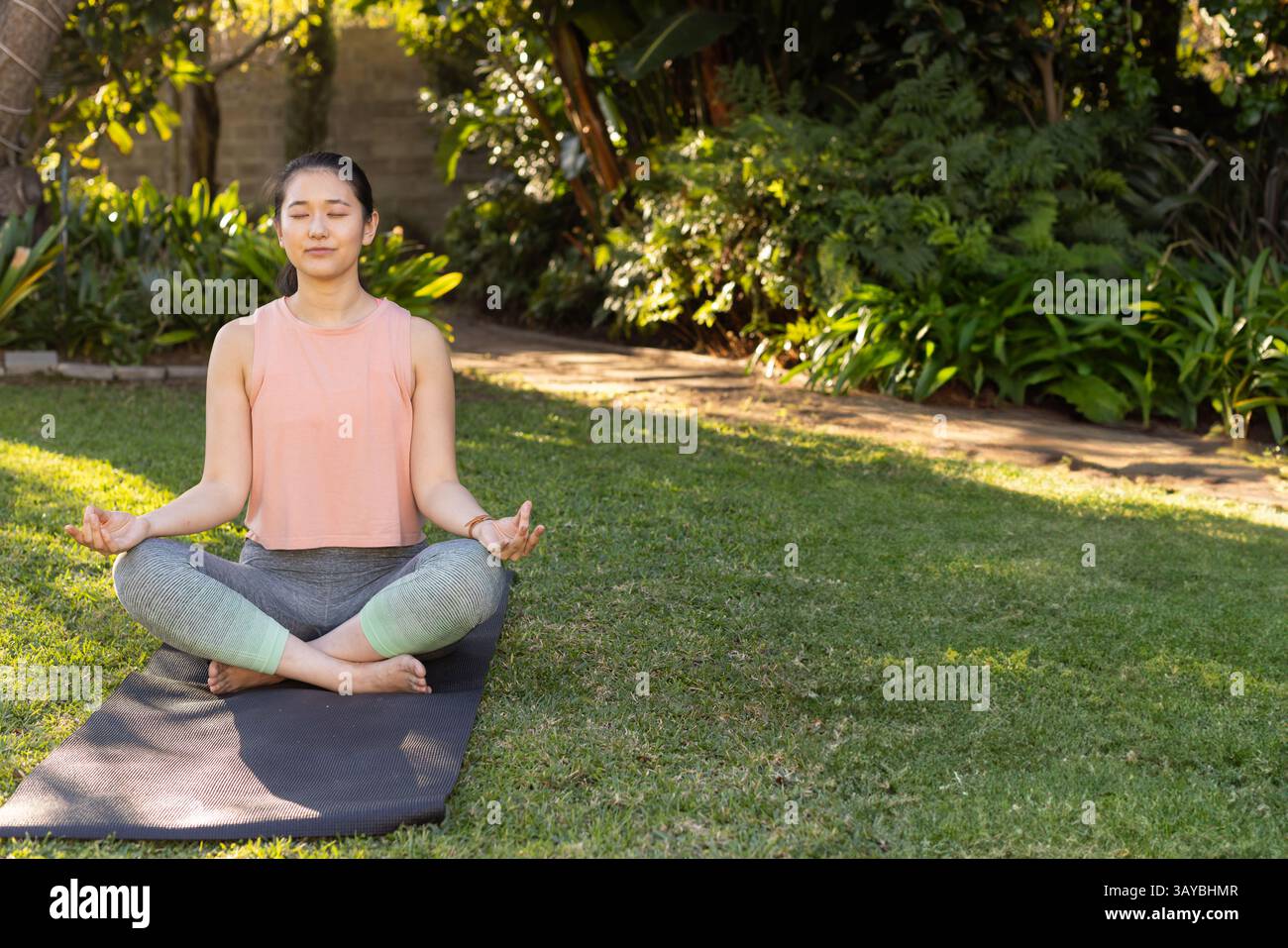 Mid-adult Asian woman sitting cross-legged on grass in backyard, using ...