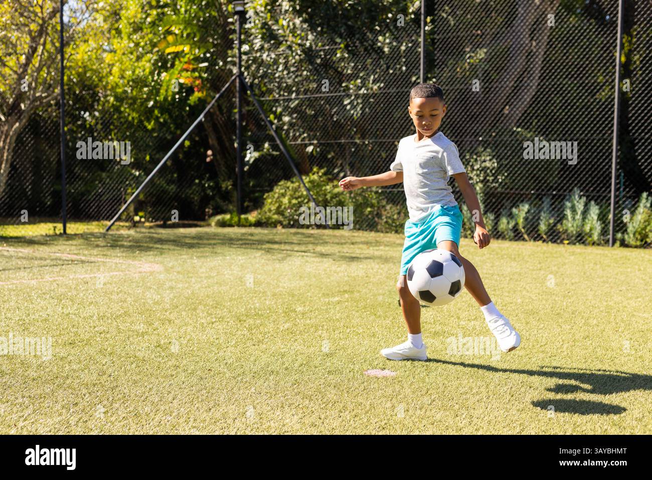 African American boy balancing soccer ball on artificial turf field ...