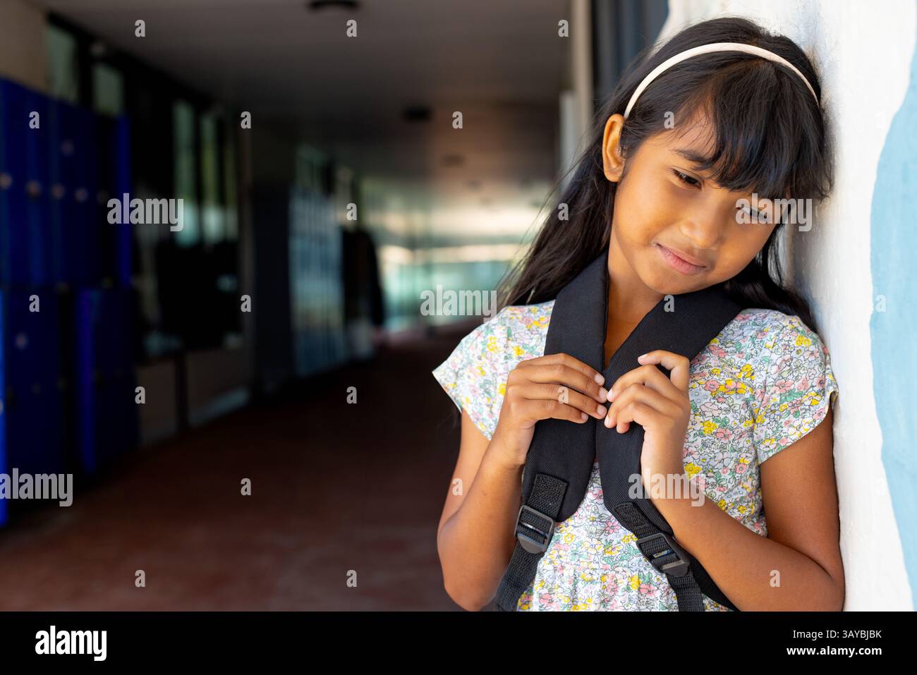 Child girl leaning against wall in school corridor, holding backpack ...